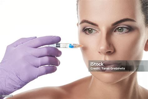 아름다운 여성의 얼굴 근처에 주사기를 들고 보라색 장갑을 낀 미용사 흰색 배경에 격리된 세로입니다 노화 방지 치료 사출 미용학 개념에 대한 스톡 사진 및 기타 이미지