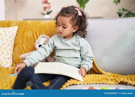 Adorable Hispanic Girl Drawing On Notebook Sitting On Sofa At Home