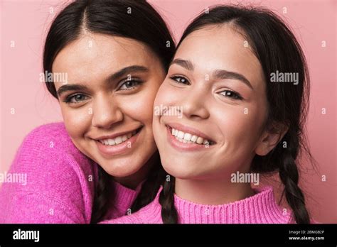 Two Cheerful Cute Teenage Girls Having Fun Isolated Over Pink Background Grimacing Hugging