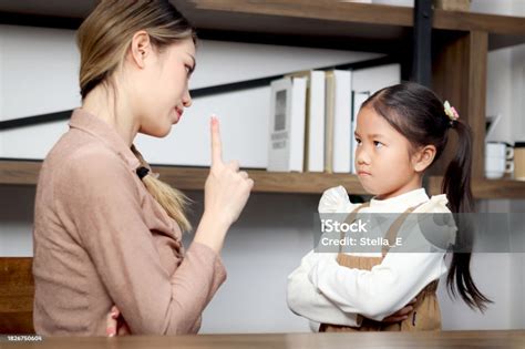 아시아의 불행한 화난 어린 딸이 팔짱을 끼고 서서 엄마가 그녀를 꾸짖습니다 엄마는 어린 소녀를 꾸짖고 아이에게 부적절한 행동에 대해 가르치고 갈등이 있는 가족 관계 아이에