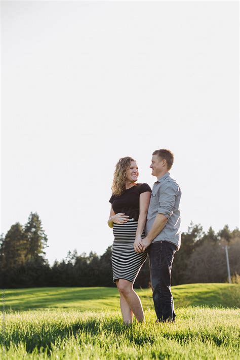 Happy Expecting Couple Together In A Field At Sunset By Stocksy