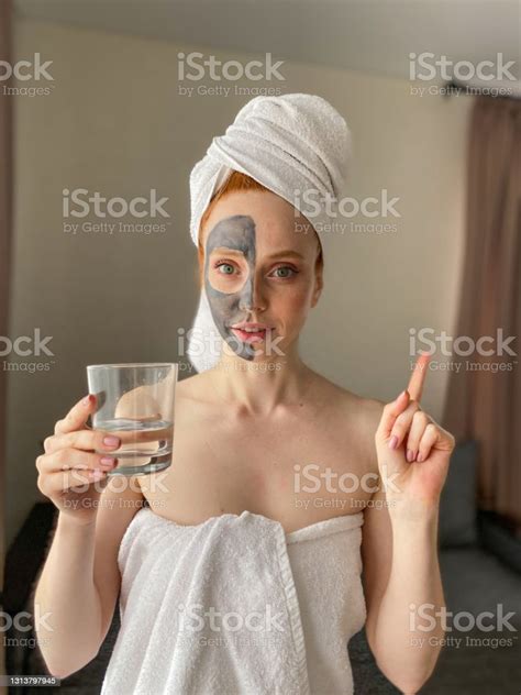 머리와 몸에 수건을 입은 한 젊은 여성의 초상화가 얼굴 의 절반에 점토 마스크를 쓰고 카메라를 향해 미소짓는 포즈를 취하고