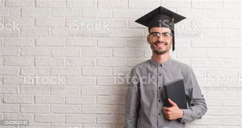 서 치아를 보여주는 자신감 미소로 웃 고 행복 한 얼굴로 졸업 모자를 쓰고 하는 벽돌 벽을 통해 젊은 성인 남자 인물 사진에 대한 스톡 사진 및 기타 이미지 Istock