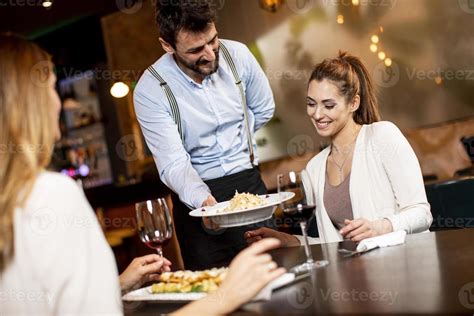 Young Waiter Serving Food To Female Customers In The Restaurant