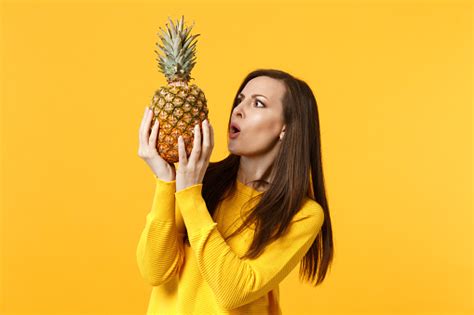 입을 열고 노란 오렌지 배경에 고립 된 신선한 잘 익은 파인애플 과일을 유지 하는 캐주얼 옷에 젊은 여자 충격 사람들은 생생한
