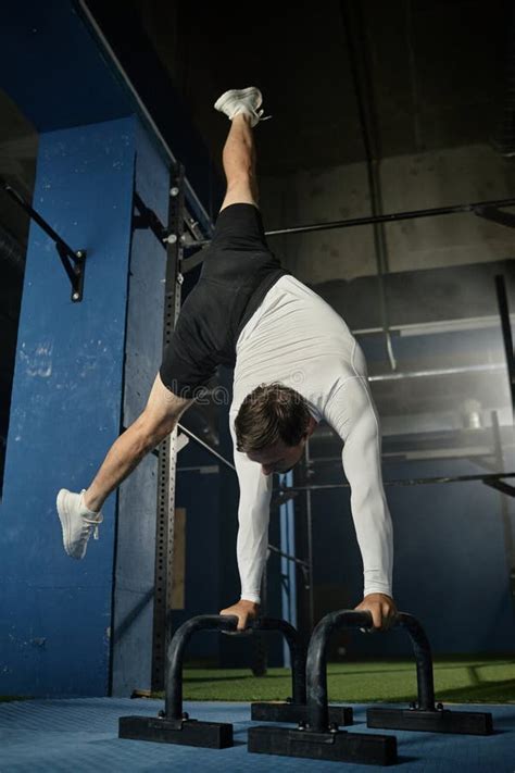 Sportsman In Handstand On Parallettes With One Leg On Side In Gym Stock