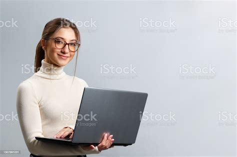 안경을 쓴 귀여운 젊은 여성이 노트북을 들고 있다 아름다운 소녀 학생은 미소와 복사 공간이있는 회색 배경에 카메라를보고 미소에