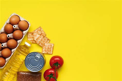 노란 배경에 있는 검역 격리 기간 동안 음식물가 비스킷 메밀 계란 토마토 통조림 상품 버터가 있는 종이 노란색 배경 복사 공간을