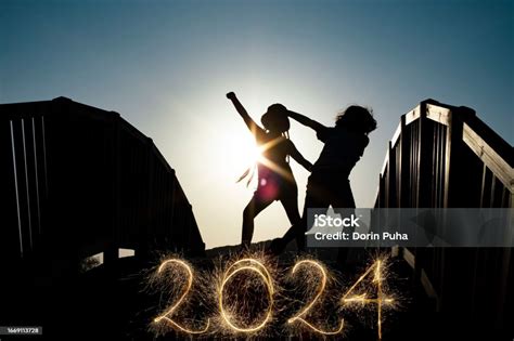 번호 2022 쓰여진 반짝이는 폭죽 휴일 인사말 카드 또는 파티를 위한 포스터를 위한 창의적인 오버레이 템플릿 해질녘에 다리 위에서 춤을 추는 소년과 소녀의 실루엣 2명에