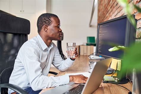 programmer drinking water while reviewing code on computer while