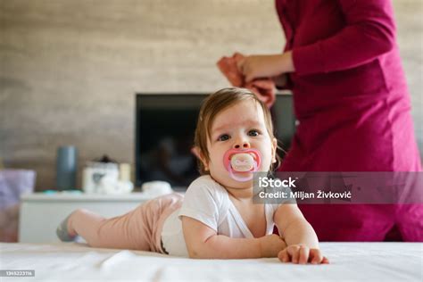 백인 아기는 그녀의 어머니가 실제 사람과 가족 개념을 변경하는 옷을 찾고 뒤에 서있는 동안 아래로 배의 밝은 방에 집에서 침대에