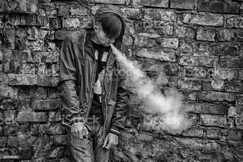 Vape 남자입니다 사진 후드 Vaping에 가까이 오래 된 전자 담배에서 증기 시키는 잘생긴 젊은 백인 남자의 붉은 벽돌 벽을