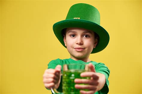 레프러펀 모자를 쓴 한 소년이 그 앞에 녹색 음료를 들고 카메라를 들고 있다 노란색 배경에서 격리됩니다 세인트 패트릭 데이 3월에 대한 스톡 사진 및 기타 이미지 Istock