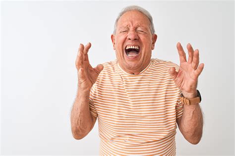 줄무늬 티셔츠를 입은 선임 회색 머리의 남자가 팔을 들고 눈을 감고 흥분을 일으키며 성공을 축하하기 위해 미친 듯이 빛나는 흰색