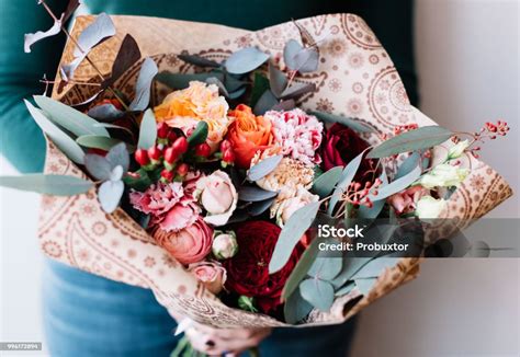 회색 벽 바탕에 파스텔 핑크와 선명한 붉은 색에 장미 핑크 라 카네이션 유 칼 리 나무의 큰 아름 다운 신선한 꽃 꽃다발을 들고 하는 아주 좋은 꽃집 여자 가까이 보기