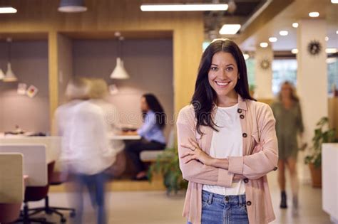 Portrait Of Businesswoman Standing In Busy Open Plan Office With Motion
