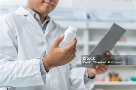 의료 약국 및 건강 관리 실험실 가운을 입은 남성 약사가 알약 병과 정제를 들고 있는 모습을 클로즈업합니다 그는 현대 약국의