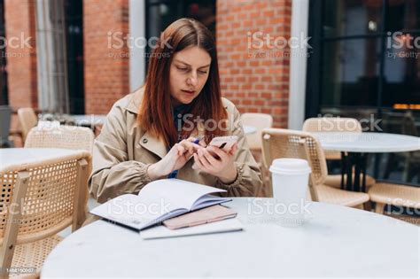 커피를 즐기며 현대 도시 거리의 카페 테라스에 앉아있는 젊은 여성 야외에 서있는 휴대 전화에서 사용하는 여성 근로자 테이블에