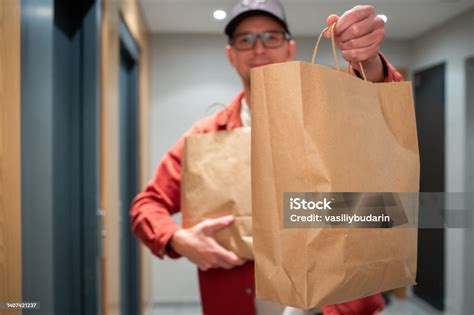 현관에 음식과 종이 봉투를 들고 배달 남자 택배는 고객에게 신선한 야채와 과일이있는 상자를 제공합니다 30 34세에 대한 스톡