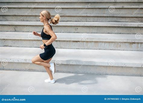 Mujer Rubia Con Ropa Deportiva Negra Corriendo Y Con Aspecto Concentrado Imagen De Archivo
