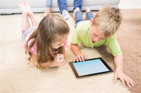 Premium Photo Smiling Siblings Lying On The Rug Using A Tablet