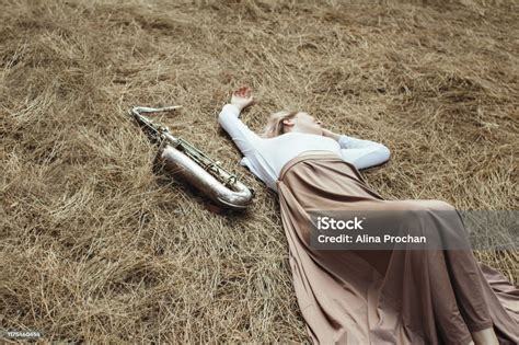 색소폰 옆에 마른 잔디에 누워 긴 드레스에 아름다운 젊은 여성의 몸 건초에 여름에 소녀는 악기 자연에 휴식의 개념과 함께 휴식