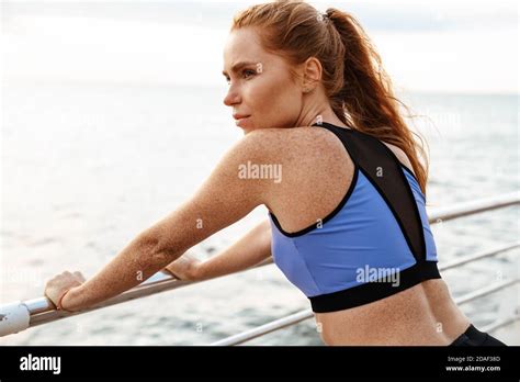 Image Of Redhead Athletic Sportswoman Doing Exercise While Working Out On Promenade Stock Photo
