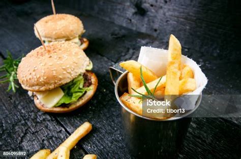 햄버거와 감자 튀김 탄 검은 나무 테이블에 패스트 푸드 식사입니다 집 햄버거를 쇠고기 고기 상 추 토마토 쓰레기통 드레싱 치즈 향신료의 구성 했다 빈티지 감자 요리에 대한