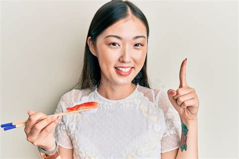 Young Chinese Woman Eating Prawn Sushi Using Chopsticks Smiling With An