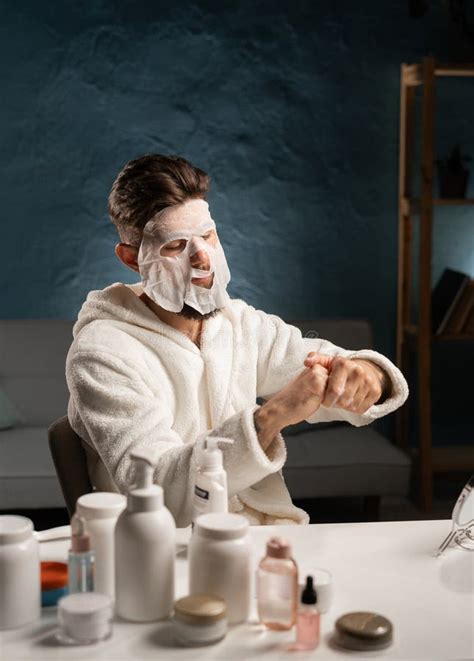 Young Man Care of His Skin at Home Applies Sheet Mask To His Face and Smears Hands with ...