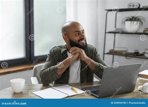 Happy Latino Man Sitting At Table In Front Of Laptop Computer At Home