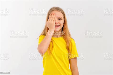 금발 머리를 가진 매력적인 십 대 소녀 손으로 얼굴의 절반을 가리고 행복한 얼굴로 카메라를 한 눈으로 바라보고 흰색 스튜디오