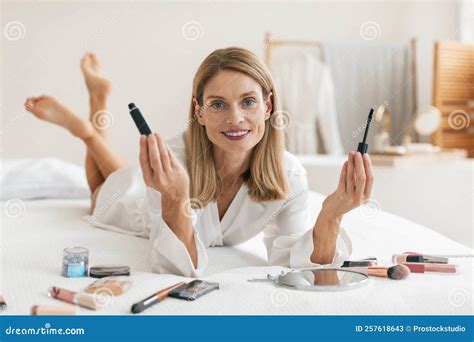 Happy Middle Aged Woman In White Robe Lying On Bed With Brush And