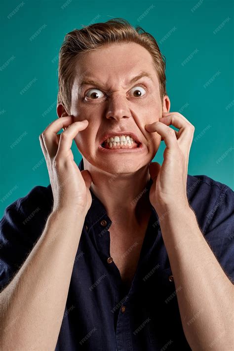 파란색 스튜디오 배경에서 포즈를 취하는 동안 화난 것처럼 보이는 세련된 해군 티셔츠를 입은 젊은 생강 남성의 클로즈업 초상화 인간의 표정 성실한 감정 개념입니다 공간을