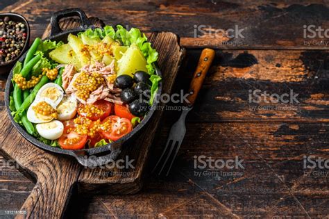 참치 체리 토마토 올리브 녹색 콩 오이 부드러운 삶은 계란과 감자를 곁들인 니코이즈 샐러드 어두운 나무 배경 맨 위 보기입니다
