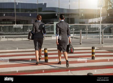 Two Flight Attendants With Bags Crossing The Road Near The Airport
