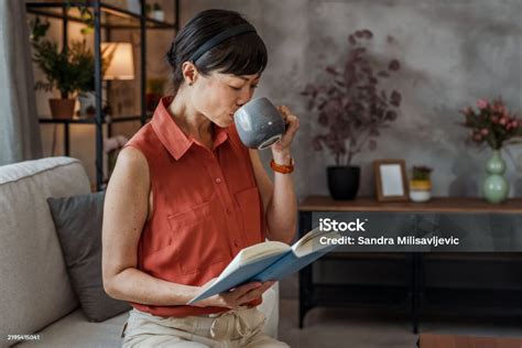 한 일본 여성이 집에서 소파에 앉아 차나 커피를 들고 책을 읽고 있다 40 44세에 대한 스톡 사진 및 기타 이미지 40 44세 가정 생활 거실 Istock