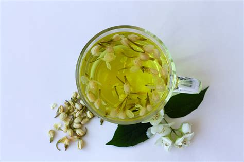 흰색 배경에 고립 된 재스민의 꽃과 허브 뜨거운 재스민 차 와 유리 컵 테이블에 말린 잎이 있는 머그잔으로 건강한 음료를