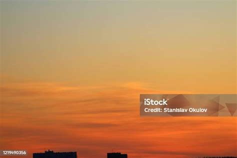 일몰이나 새벽에 태양에 의해 백라이트 에 불타는 극적인 오렌지 하늘에 배경 구름에 다층 도시 건물의 수평선과 지붕 아래 태양