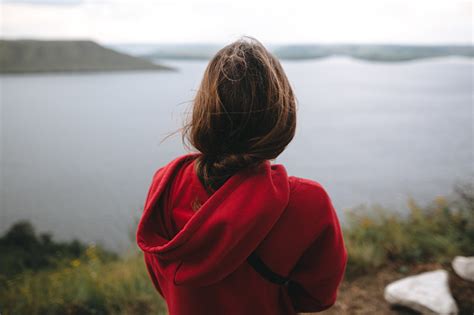 빨간 윈드 브레이커와 강이 아름다운 바위 산 꼭대기에 서있는 바람이 부는 머리카락을 가진 힙스터 소녀 분위기 진정 순간 여행과 명상 복사 공간 강에 대한 스톡 사진 및 기타