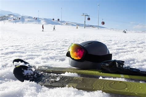 산악 스키 스키 스틱 스키 리프트와 푸른 하늘이 있는 스키 슬로프를 배경으로 밝은 고산 눈 위에 자외선 차단제 마스크가 있는 스키 헬멧 겨울 방학 익스트림 스포츠 휴가 여행