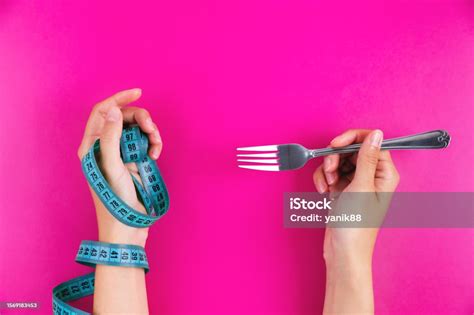 밝은 분홍색 배경에 포크와 줄자를 손에 들고 있다 줄자로 손을 묶고 포크를 들고 있는 여자 클로즈업 가냘픈에 대한 스톡 사진 및