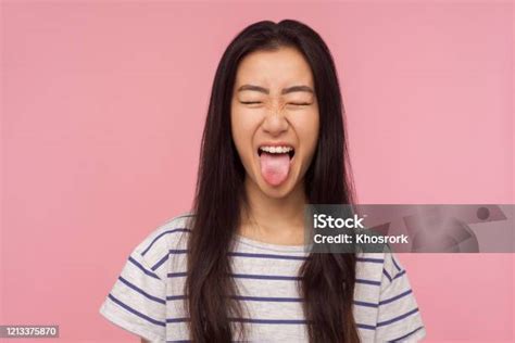 혀를 보여주는 줄무늬 티셔츠에 긴 머리를 가진 재미있는 소녀의 초상화와 장난 꾸러기 유치한 찡그린 얼굴로 눈을 감고 유지 여성에