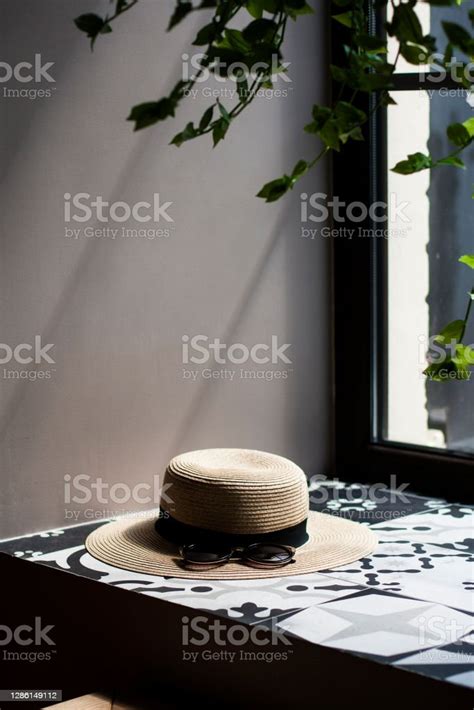검은 색 줄무늬와 선글라스가 달린 예쁜 여성용 비치 모자가 창문 틀에 누워 있고 녹색 식물과 창문이 배경에 놓여 있습니다 0명에