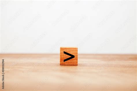 の記号。大なり。不等号。比較演算子。木製ブロックに書かれている。黒い文字。木製テーブルの背景。 Photos Adobe Stock