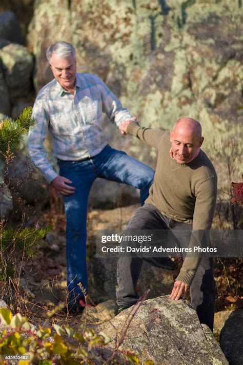 Mature Gay Couple Holding Hands While Hiking Over Rocks On Nature Trail