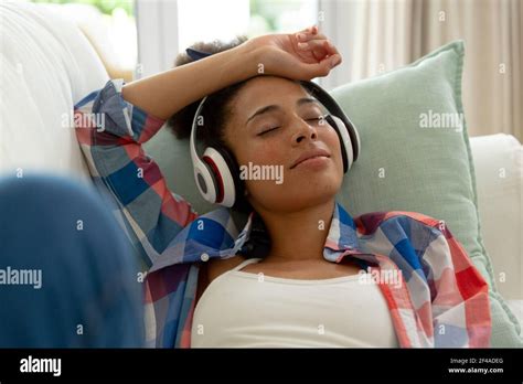 Mixed Race Woman Lying On Couch Listening To Music With Headphones At