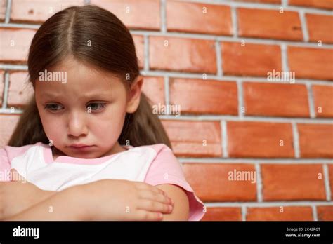 Petite fille à poil brun se tient shyly devant un mur de brique