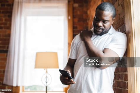 벽돌 벽에 기대어 서서 어깨를 긁고 스마트 폰을 스크롤하는 남자 흑인 민족에 대한 스톡 사진 및 기타 이미지 흑인 민족