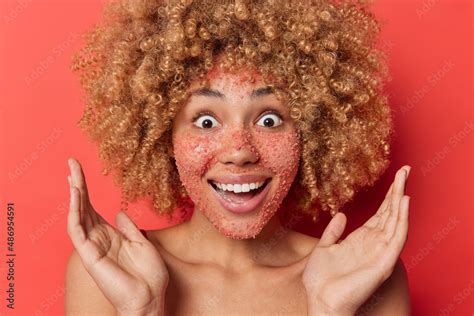 Surprised Excited Curly Haired Woman Applies Scrub On Face Poses Half Naked Spreads Palms And